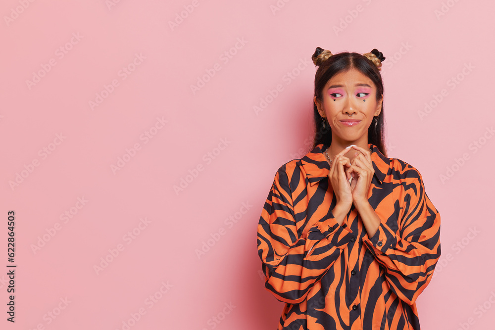 Oriental girl with two buns hairstyle pressing her hands to her chest ...