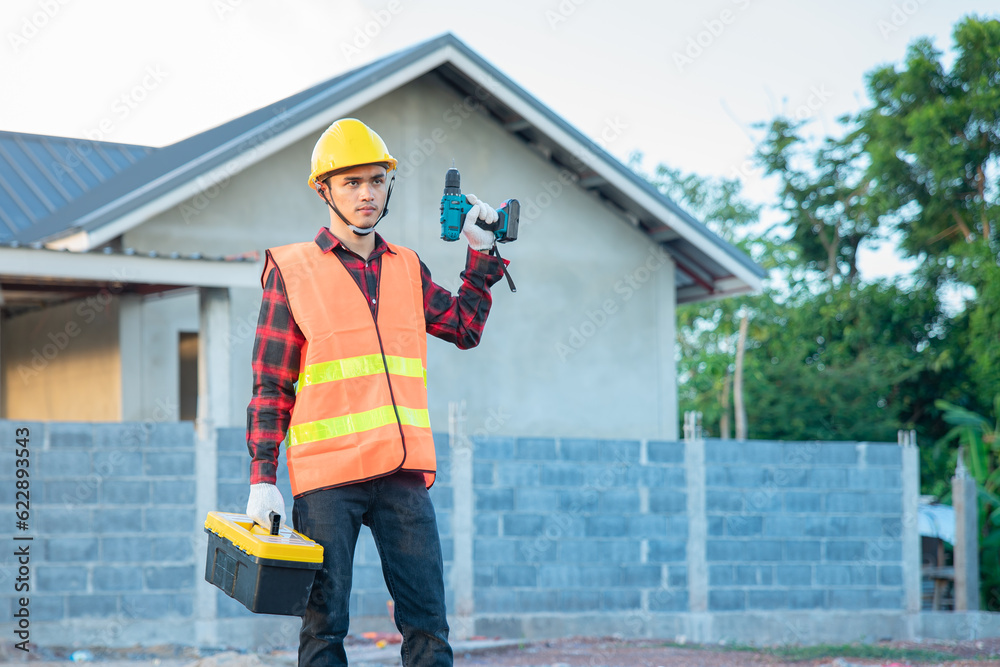 Technician wearing yellow hard hat hand holding a drill and a toolbox ...
