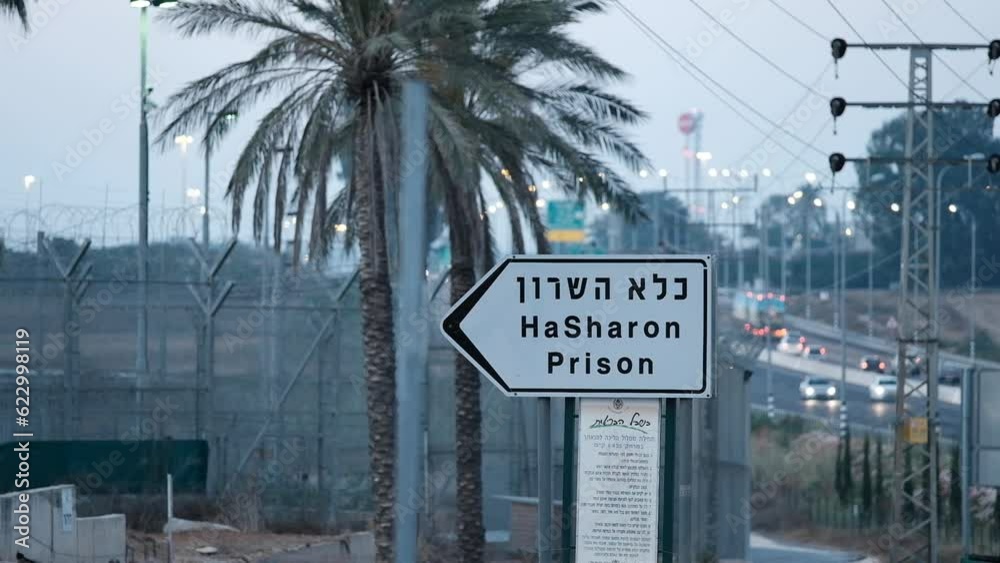 A sign of a prison and the name, with an out of focus highway in the ...