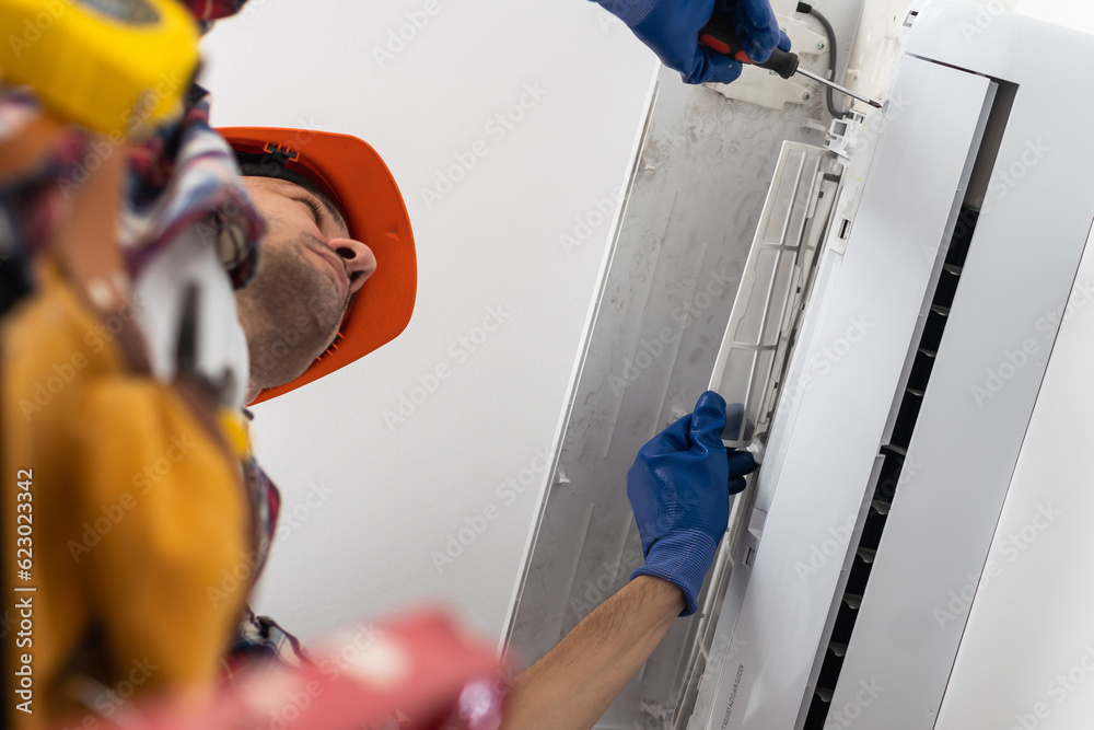 Worker installing or repairing air conditioner. Young man in uniform ...