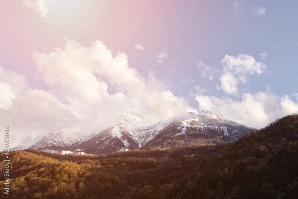 Cumulus clouds move over snowy peaks of high mountains illuminated by ...
