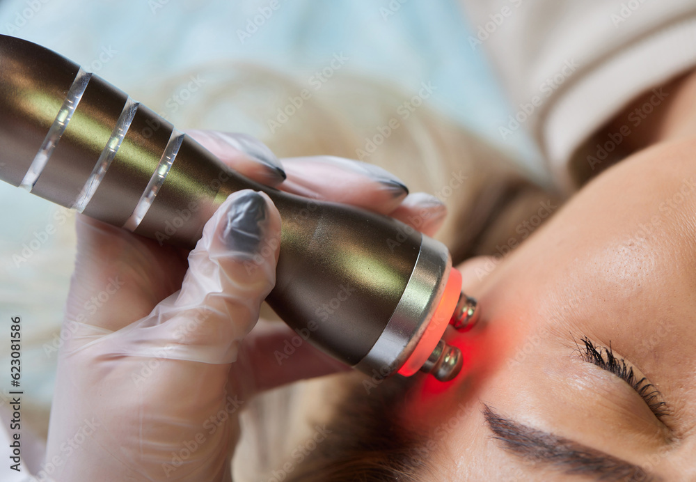A cosmetologist in rubber gloves does the rf-lifting procedure on the ...
