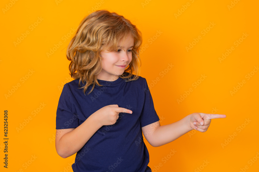 Child boy pointing finger away on yellow isolated studio background ...