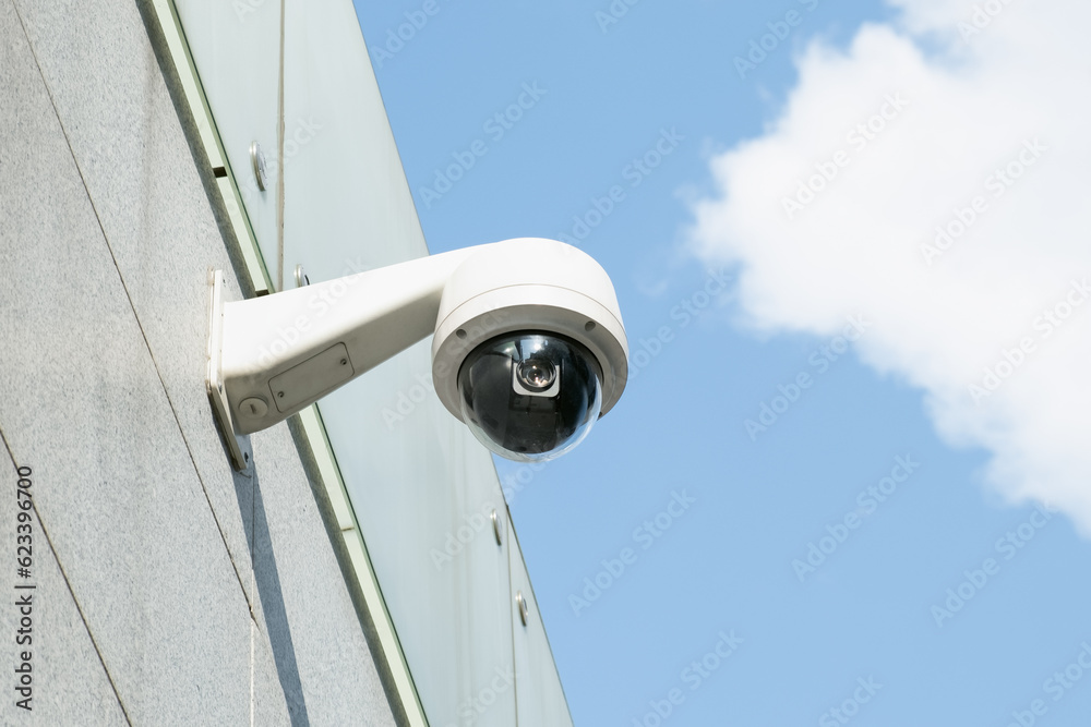 white CCTV camera camera on the wall of building against a blue sky . Security, video ...