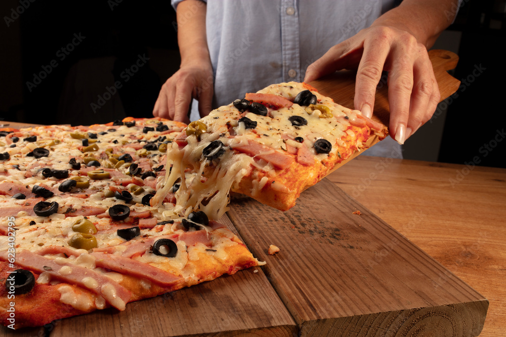 Manos partiendo una pizza de jamón, queso y aceitunas, comida italiana ...