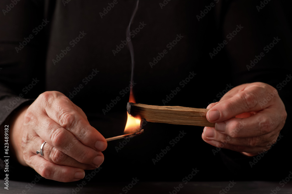 hands of a woman lighting a palo santo (holy stick) with a match with ...