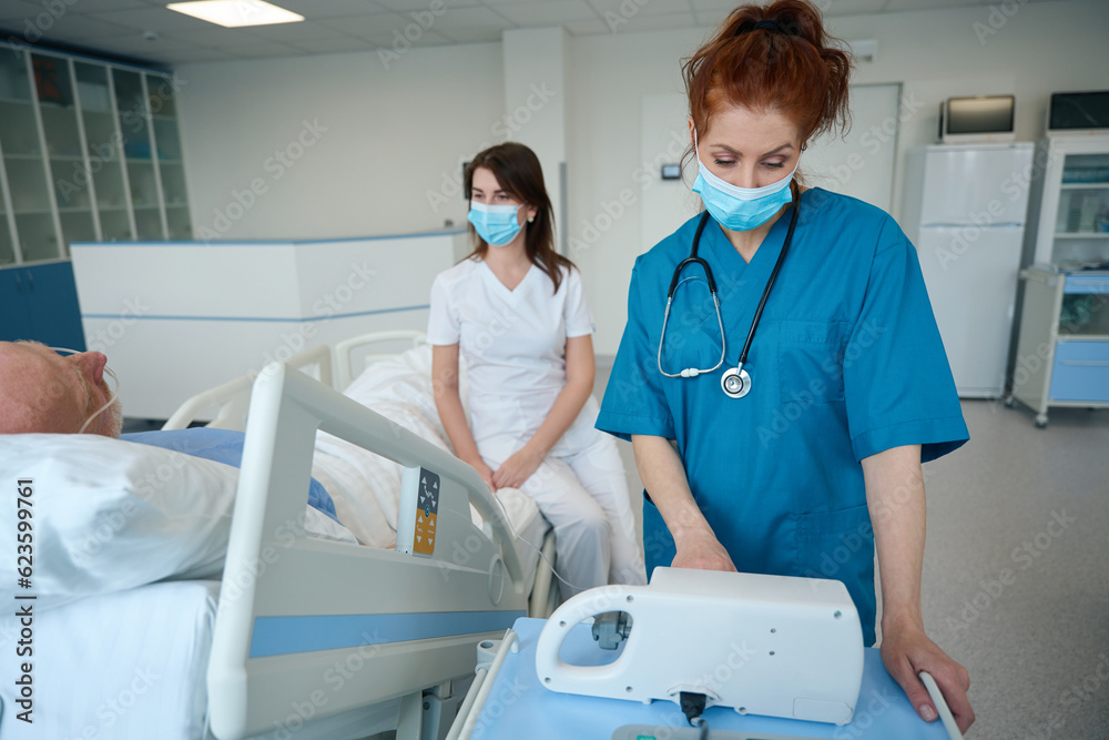 Nurse adjusting syringe pump and doctor near patient on bed in ...