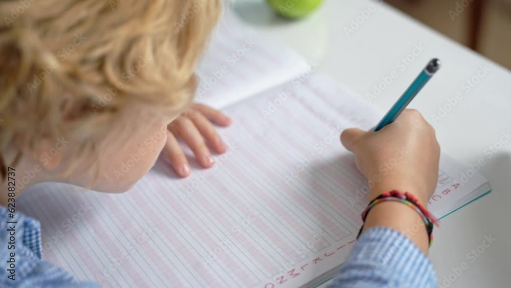 Elementary school student boy or girl writing letters, studying at desk ...