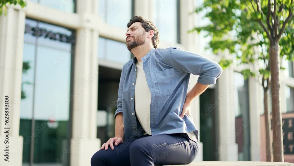 Tired man having severe back pain ache sitting on bench near modern ...