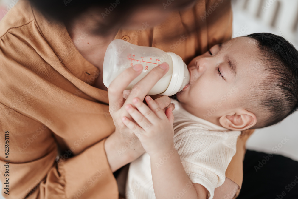 Adorable little Asian baby sleep during drinking milk from baby bottle. Mother holding adorable ...
