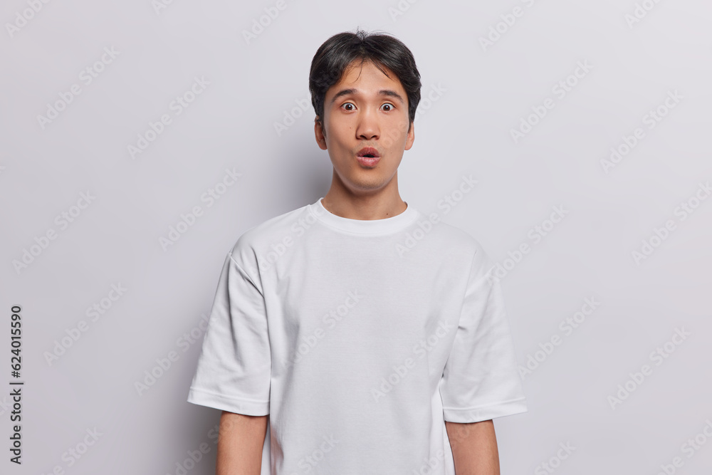 Waist up shot of stunned Asian man with dark hair stands impressed ...