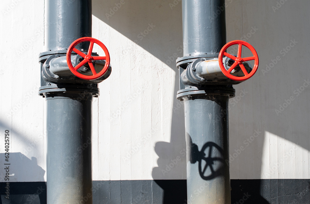 Two black pipes with red wheel in front of white wall. With sharp ...