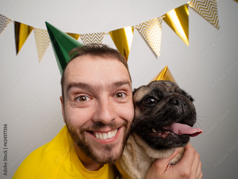 portrait of Funny guy with cute pug dog in a party hat hugging and ...