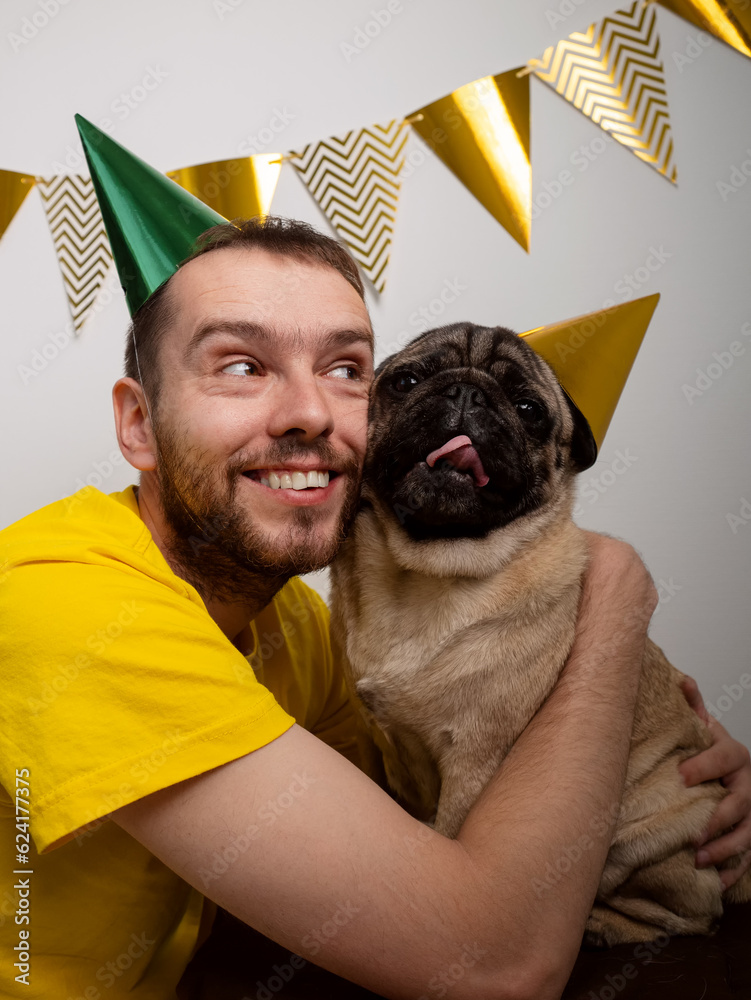 Funny guy with cute pug dog in a party hat hugging and celebrating pet ...