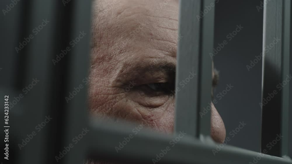Face close up of angry elderly prisoner standing behind metal bars in ...