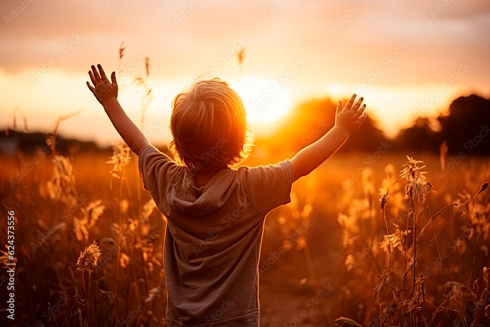 A little boy raises his hands above the sunset sky, enjoying life and ...