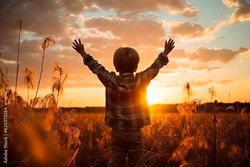 A little boy raises his hands above the sunset sky, enjoying life and ...