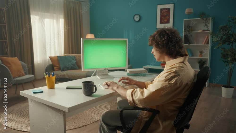 A young man drinks morning coffee and works at a computer with a green ...