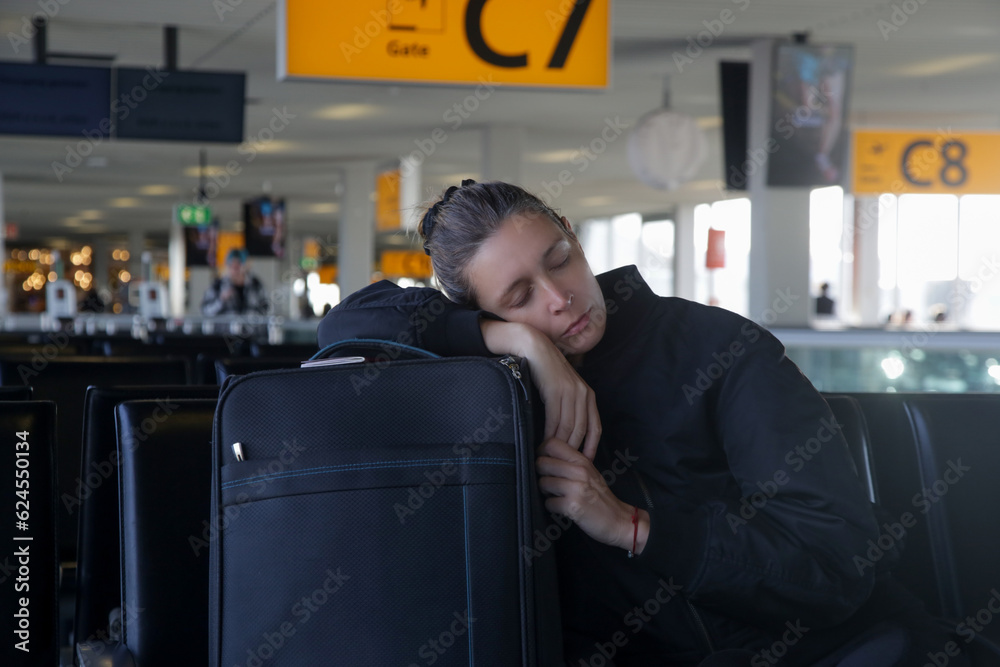 Tired tourist woman sleeping on luggage while waiting for her flight at ...