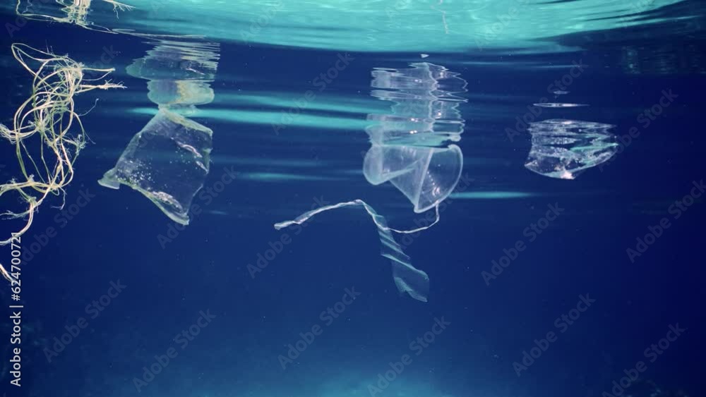 Plastic debris floating below surface in blue water, Slow motion ...