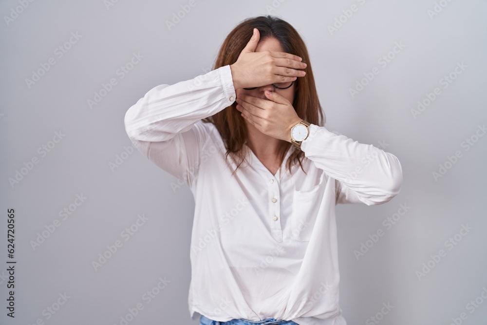 Brunette woman standing over white isolated background covering eyes ...