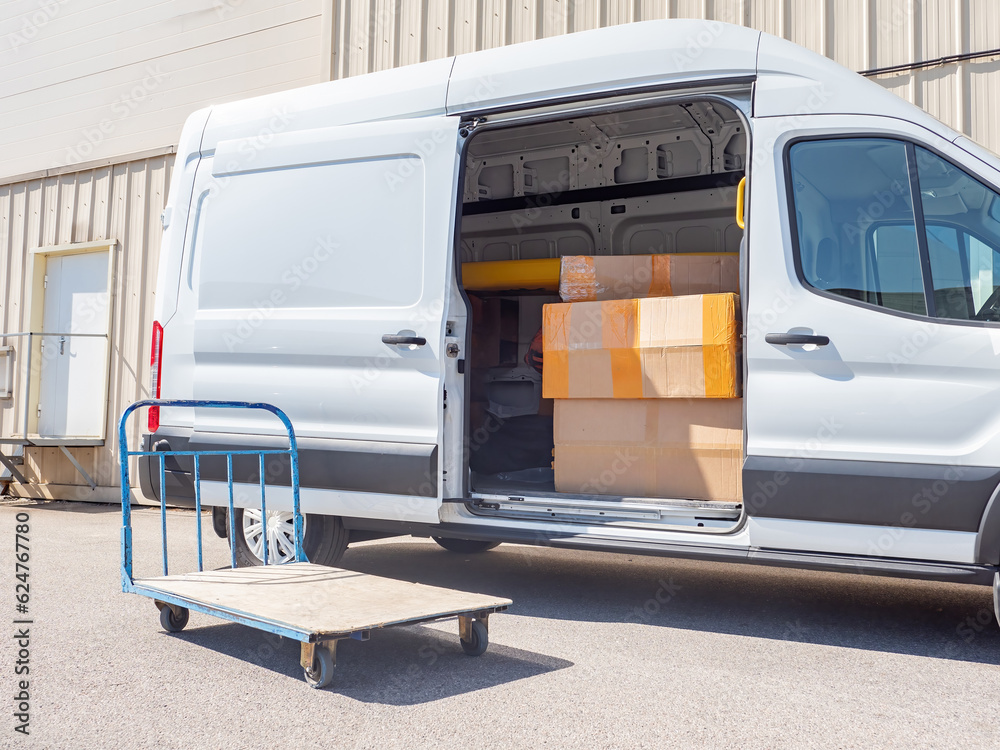 Minivan with boxes. Delivery service car. Cargo cart next to minivan ...