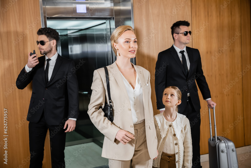 successful mother and child holding hands while standing near hotel ...