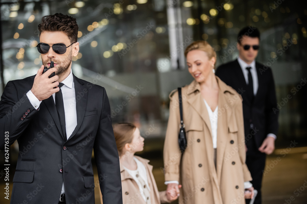 handsome bodyguard communicating through walkie talkie, standing next ...