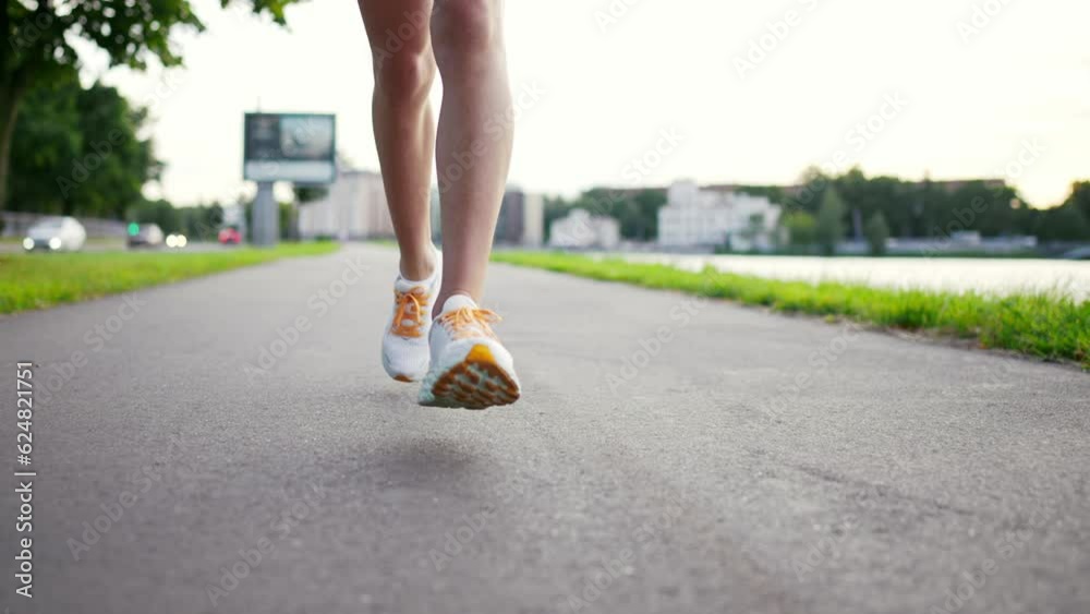 Legs of woman in white sneakers running on walkway in city park near ...