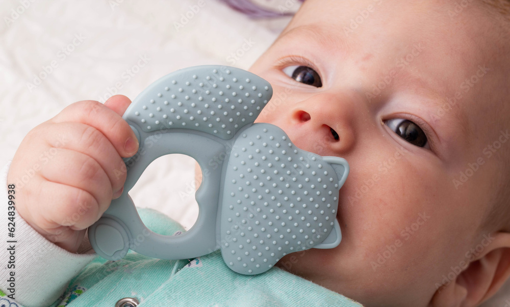 A baby caucasian boy plays with a teether during the eruption of the ...