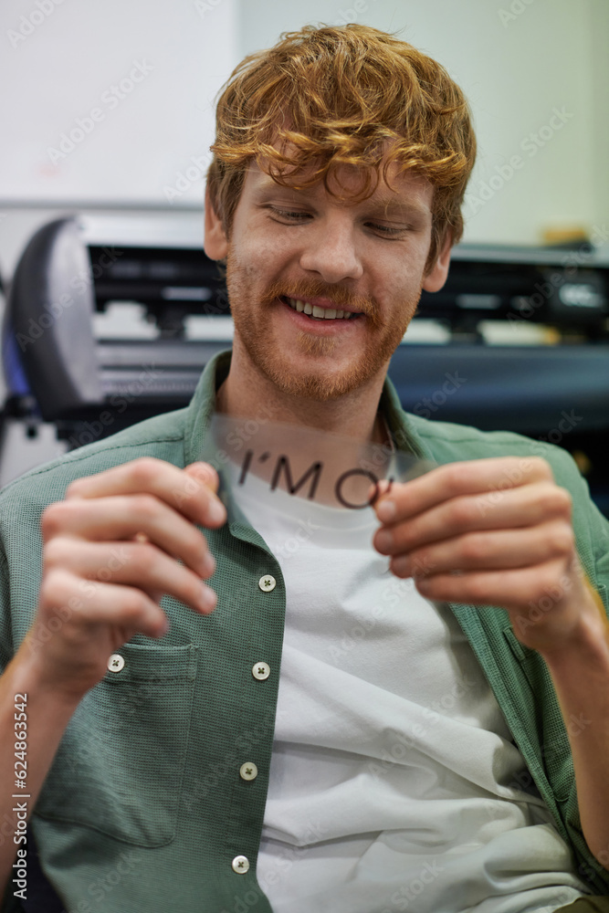 Smiling young redhead craftsman holding layer with I'm ok lettering ...