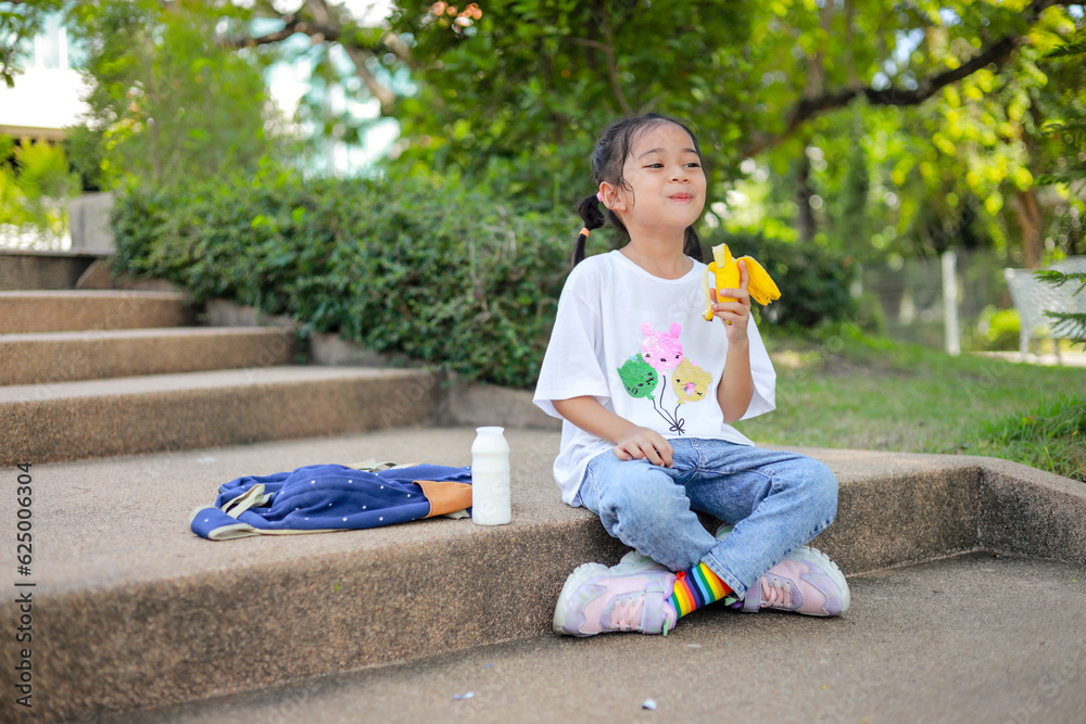 Little kid girl asian holding and eat banana in the school. feel happy ...