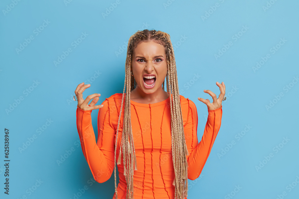 Young angry woman with long dreads dressed in orange top on blue ...