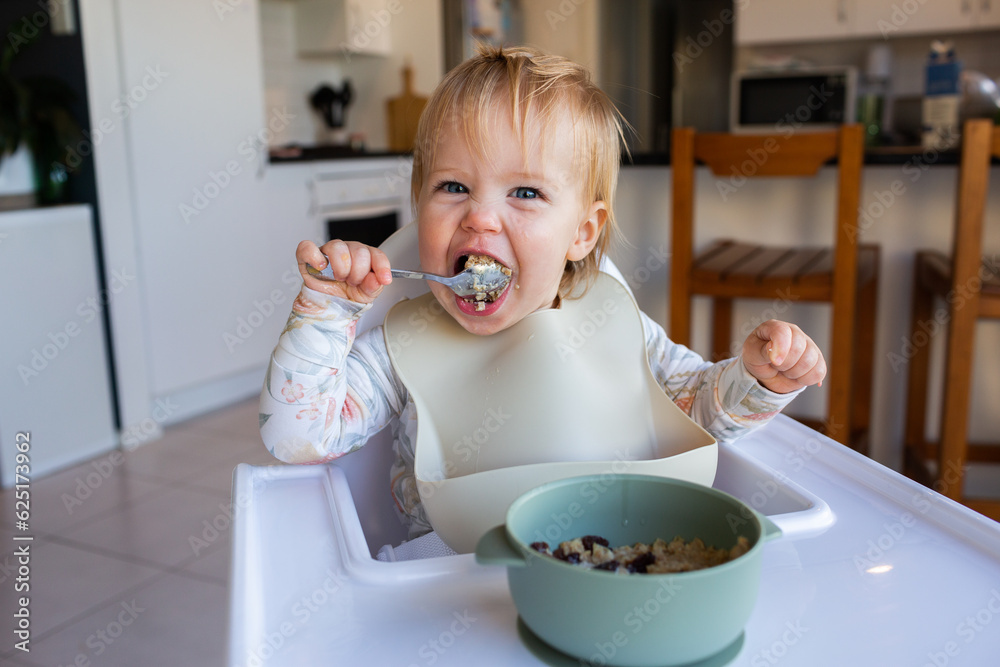 One year old baby girl using spoon to eat weetbix and sultanas for ...