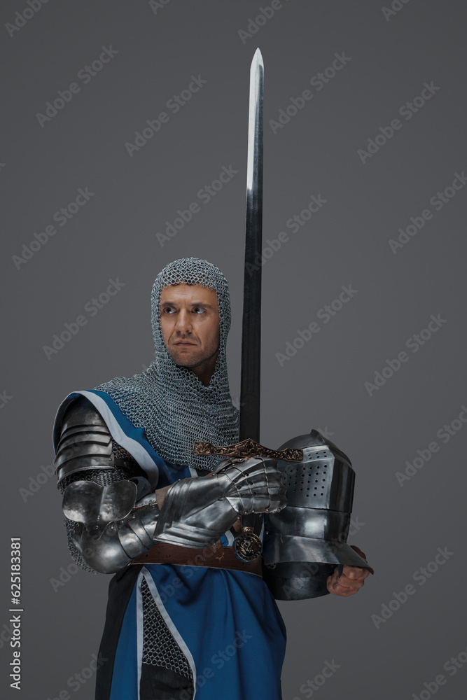 Proud knight stands holding his sword and helmet, donning blue surcoat ...