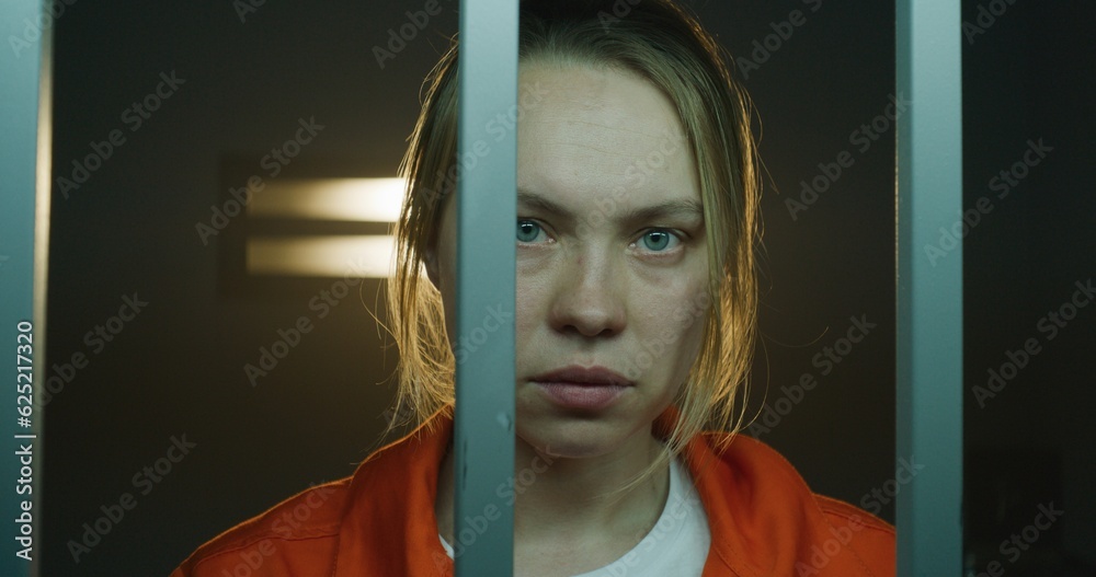 Scared female prisoner in orange uniform holds metal bars, stands in ...