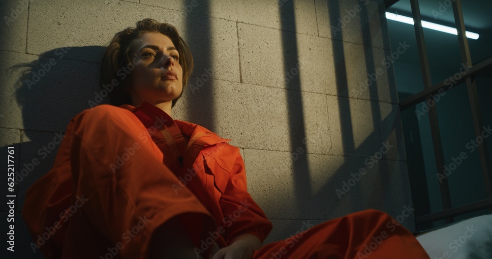 Female prisoner in orange uniform sits on bed in prison cell, reads ...