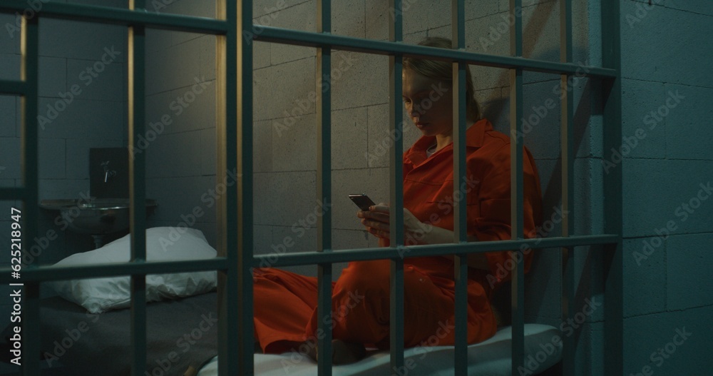 Female prisoner using smartphone in prison. Woman criminal in orange ...