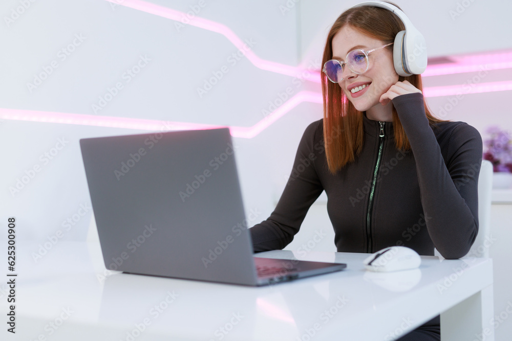 Gamer girl works and plays at the computer. Female in modern headphones ...