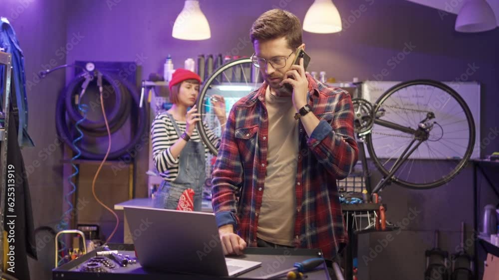 Male workshop manager talking by phone and working with laptop. At ...