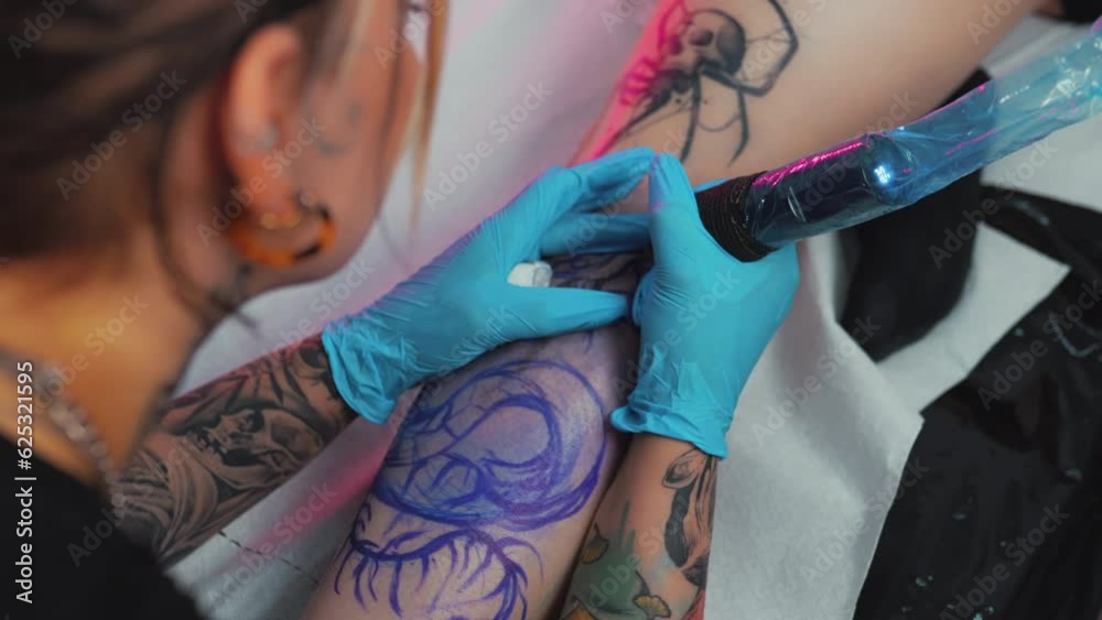 Tattoo artist doing tattoo on client leg in salon closeup tattoo making ...