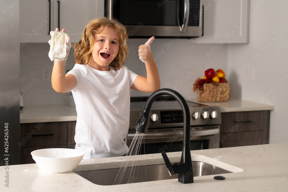 Kid washing dishes in the kitchen interior. Child helping his parents ...