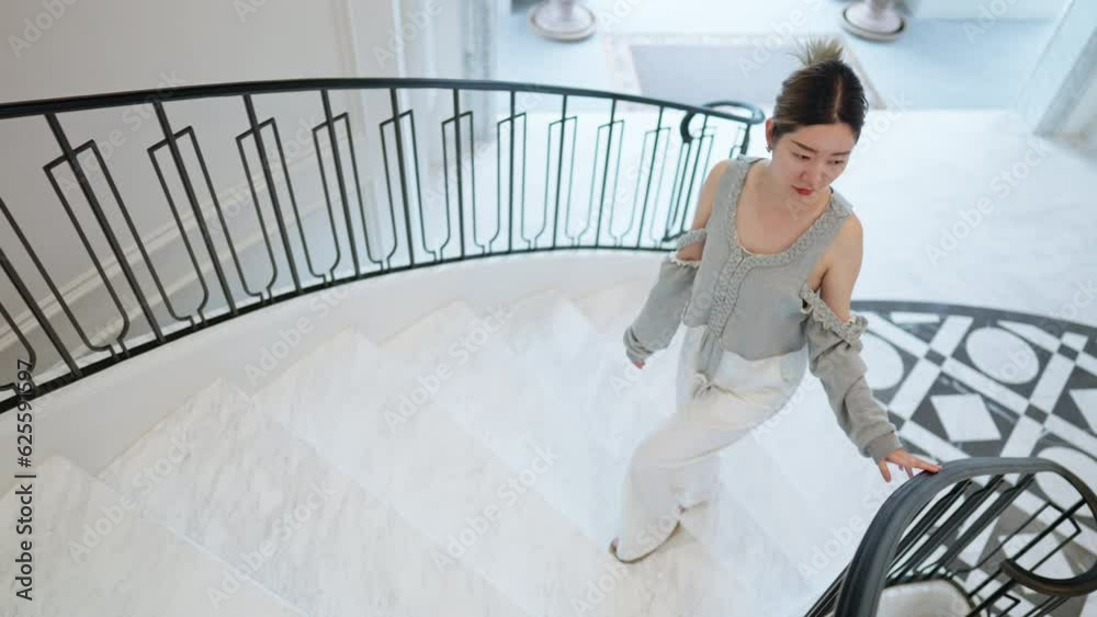 a woman ascends a luxurious staircase as the camera captures the scene ...