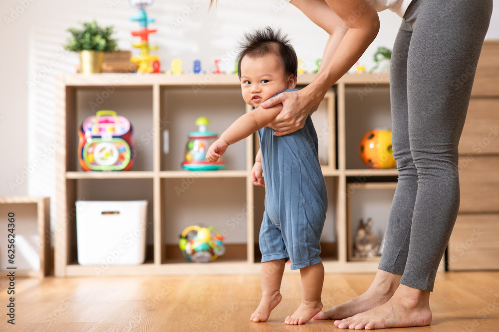 Mom helping and support baby learn to walk with love indoors at home ...
