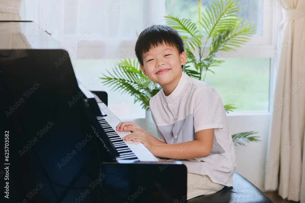 Cute happy smiling little Asian kid boy playing piano in living room at ...