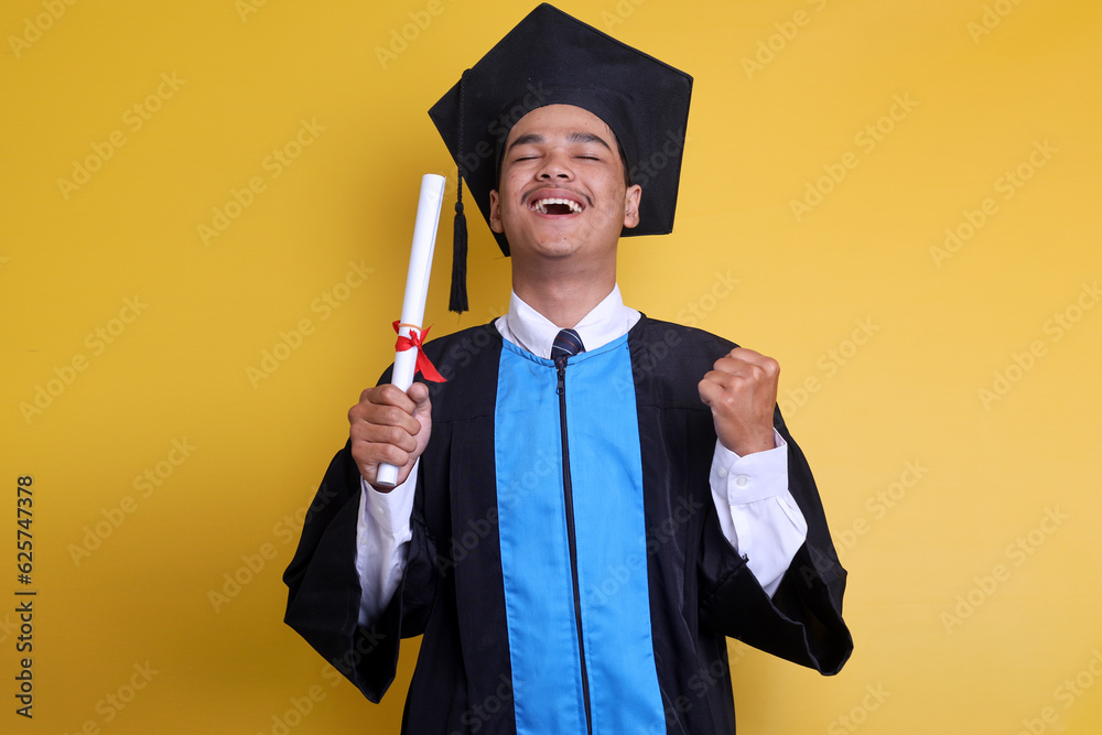Excited man in graduation cap and ceremony robe clenching his fist and ...