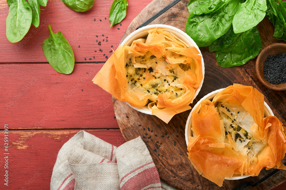 Filo pies with soft feta cheese and spinach in ceramic molds on old red ...