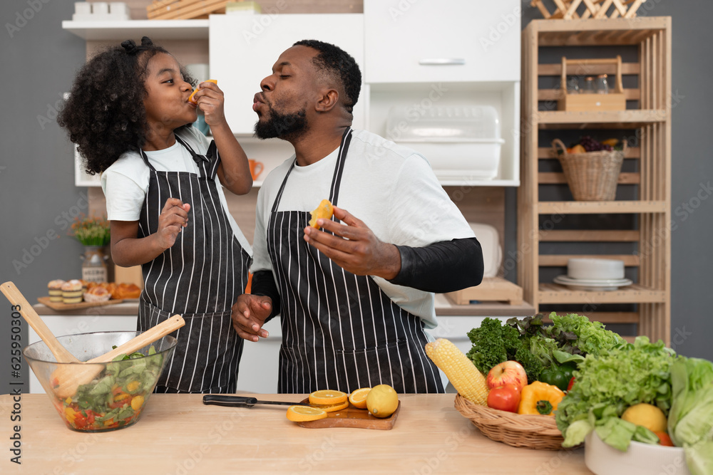 Happy African American kid girl cooking salad with father in kitchen at ...