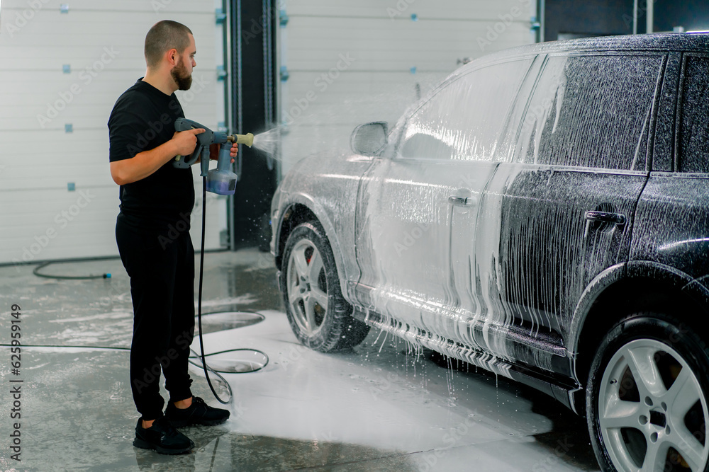 A male car wash employee applies car wash foam to a luxury black car ...