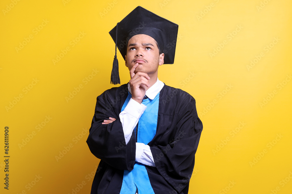 Thoughtful face of young male wearing graduation cap and ceremony robe ...